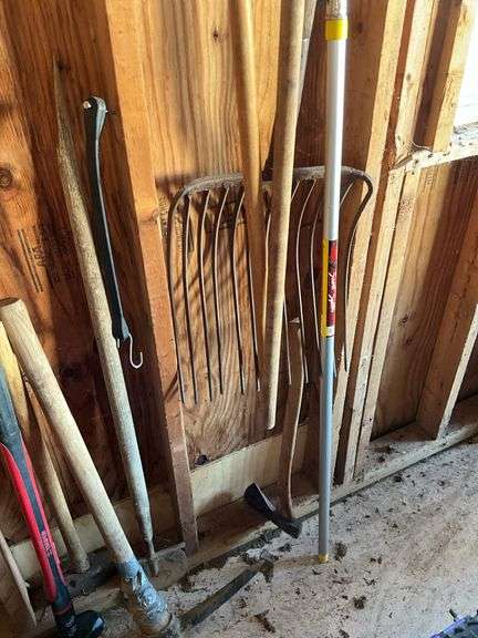 Garden tools and others hanging on wall and on floor: rakes, pick ...