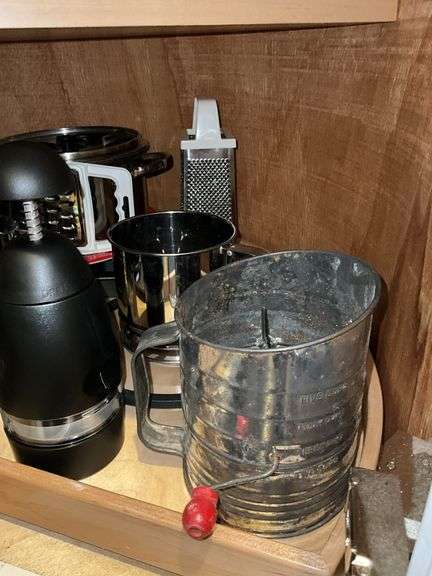 Contents of cupboard: enamel colander, cookware, stainless bowls, tube pan, misc kitchenware ...