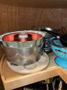 Contents of cupboard: enamel colander, cookware, stainless bowls, tube pan, misc kitchenware ...